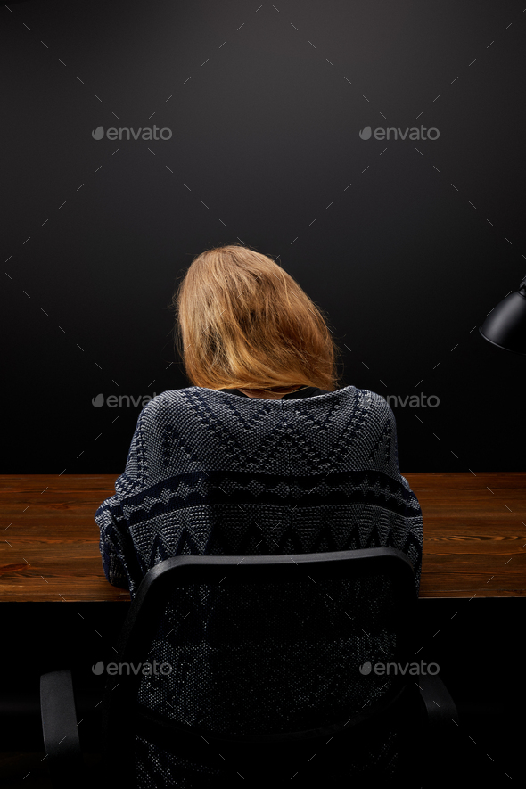 back view of woman sitting at wooden tabletop with black wall backdrop ...