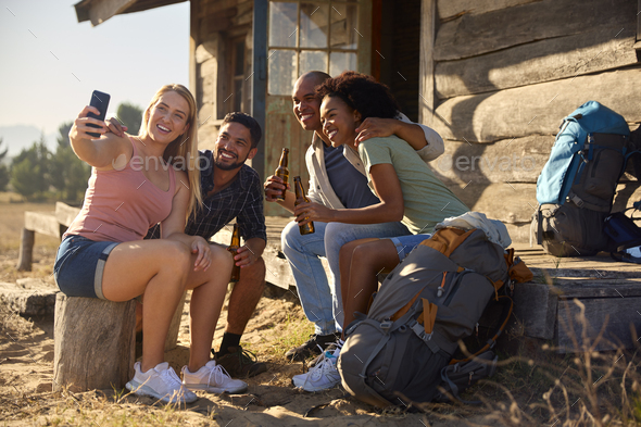 Group Of Friends On Vacation Sitting On Porch Of Countryside Cabin ...