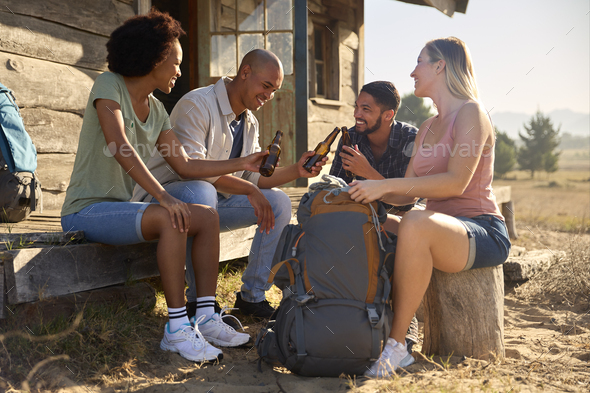 Group Of Friends On Vacation Sitting On Porch Of Countryside Cabin ...