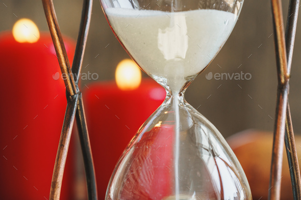 Hourglass and red burning candles close up Stock Photo by FabrikaPhoto