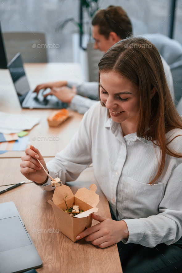 Two coworkers are eating food that is in the eco boxes. Sitting in the ...