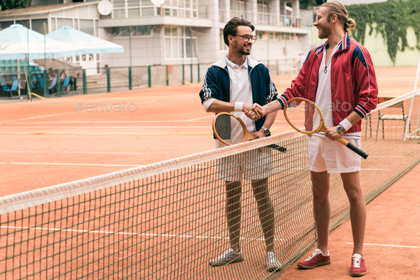 friends with wooden rackets shaking hands on tennis court with net ...