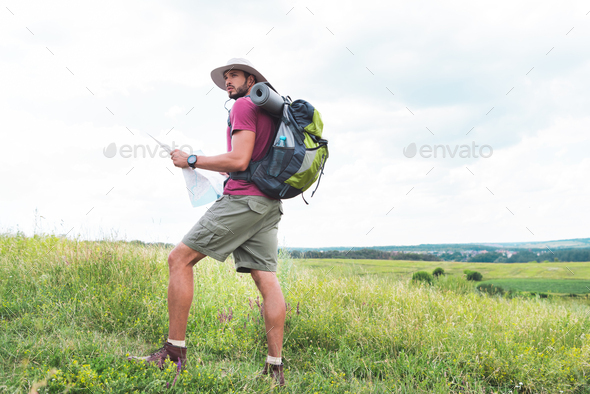 hiker with backpack holding map and standing on green field Stock Photo ...