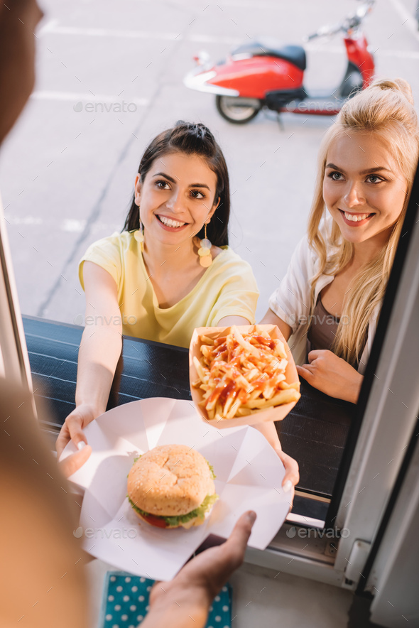 cropped image of chef giving burger and french fries to smiling ...