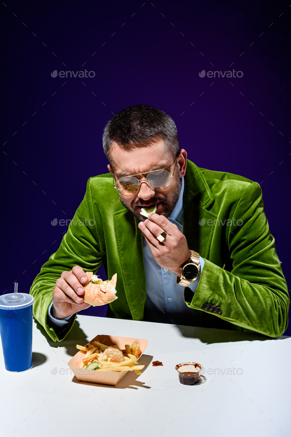 portrait of man in velvet jacket eating burger at table with french ...
