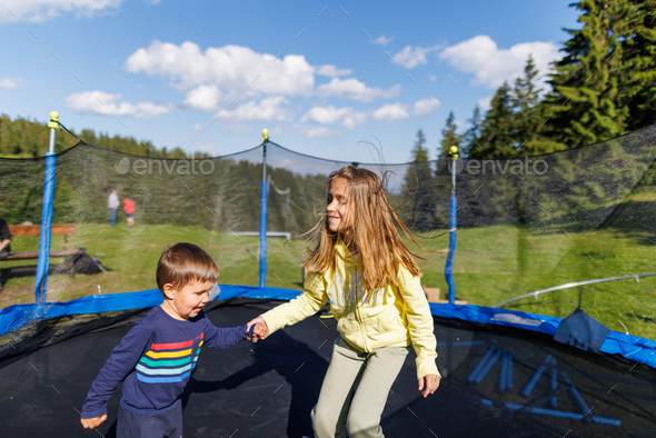 Older sister and her little brother are jumping together on a netted ...