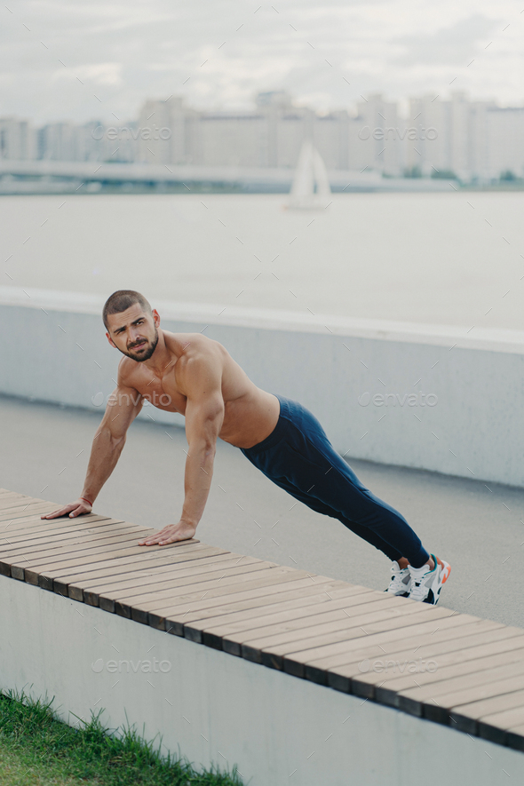 determined muscular man warms up before training stands in plank pose ...
