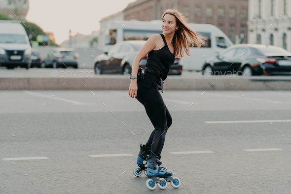 active young woman in good physical shape rollerblades along city ...