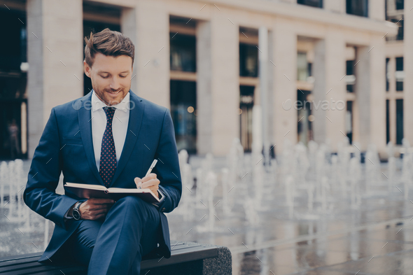 Formally dressed office worker organising his day in note book while ...