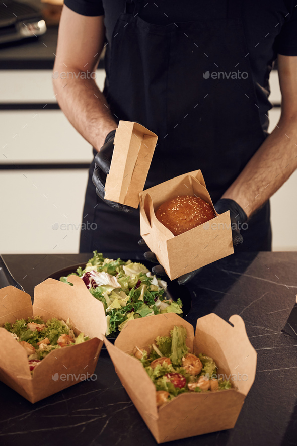 Opening the box with burger. Man is packing food. Indoors, restaurant ...