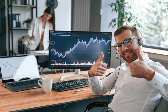 Man showing thumbs up. Graphs on the screen. Two employees are working ...