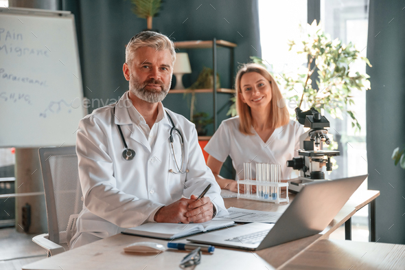 Laptop and microscope are on the table. Two clinic workers are indoors ...