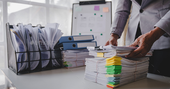 work from office A businessman works a bunch of paper files to find ...