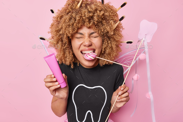 Horizontal shot of cheerful curly haired young European woman bites ...