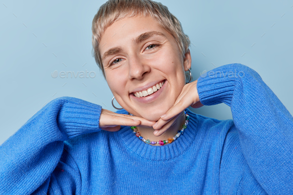 Headshot of positive short haired woman keeps hands under chin smiles ...