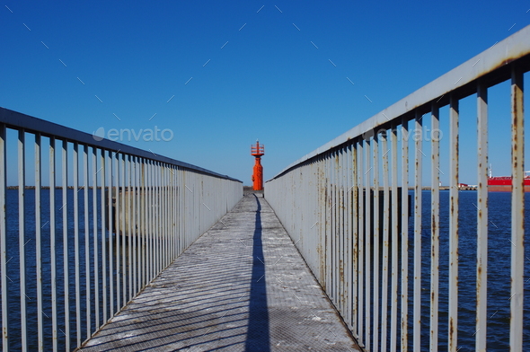 Long, narrow metal bridge on the sea leading to a giant gas tank under ...