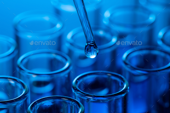 Closeup shot of a pipette tip with a droplet over glass test tubes ...