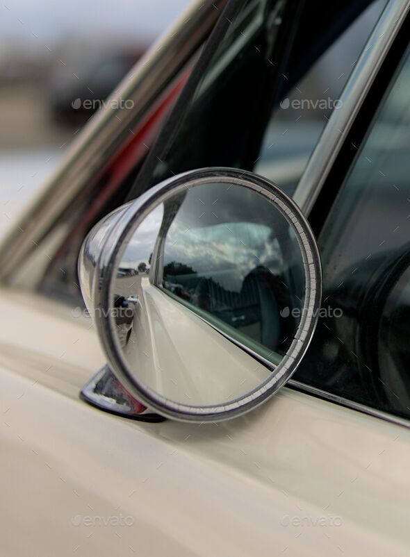 Vertical closeup of the round wing mirror of a vintage white carshowing ...