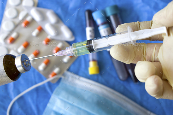 Hand in glove holding syringe and vial with drugs, test tubes, and mask ...