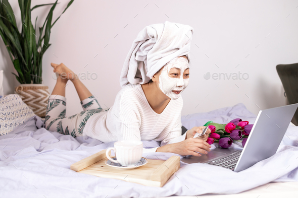Chinese woman wearing facial mask enjoying at home and using her laptop ...