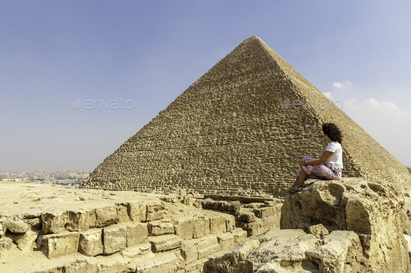 Woman sitting on a rock looking at the great pyramid of giza in egypt ...