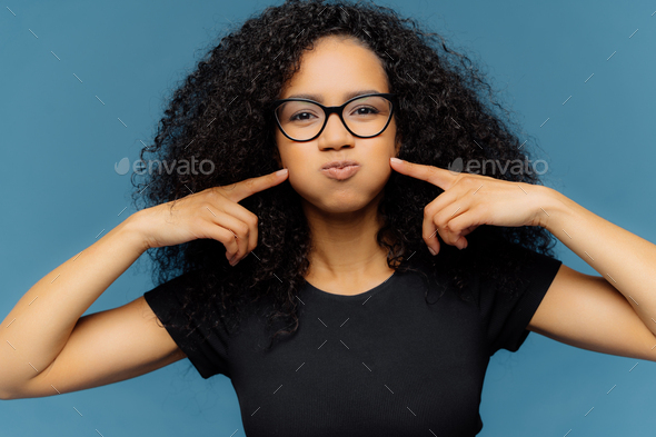 Funny dark skinned woman with curly hair, presses cheeks, holds breath ...