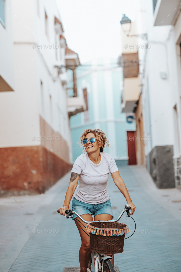 Happy cheerful young woman riding bike in the street in town with smile ...