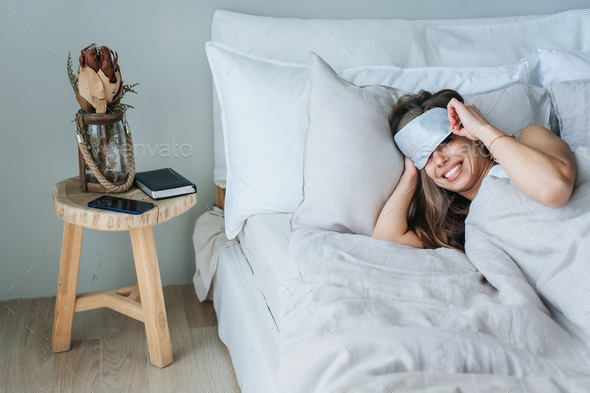 Awakening young woman laying on bed. Smiley caucasian girl takes off ...
