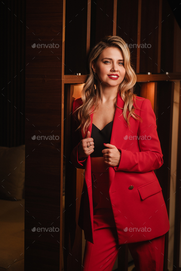 a beautiful girl dressed in a red formal suit posing in a modern ...