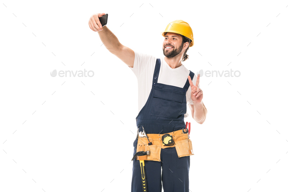 happy handsome workman in hard hat and tool belt taking selfie with smartphone isolated on white ...
