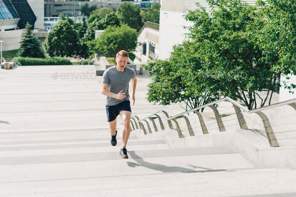 Young athlete man runner running up and down on city stairs in summer ...