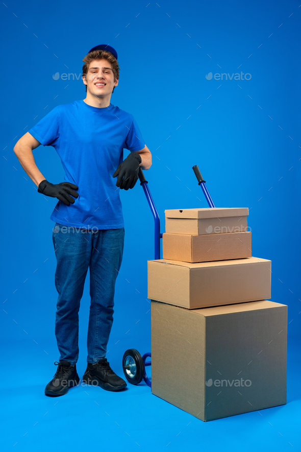 Young happy delivery man carrying boxes on truck against blue ...