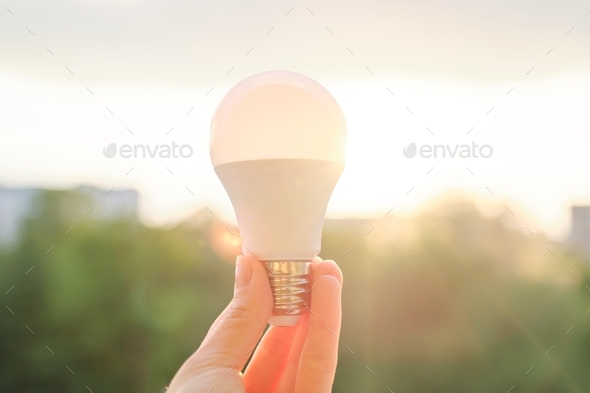 Led bulb, hand holding lamp, evening sunset sky background Stock Photo ...