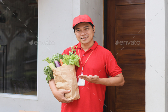 Handsome Asian delivery man carrying package box of fresh vegetable ...