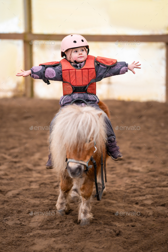 Little Child Riding Lesson. Three-year-old girl rides a pony and does ...