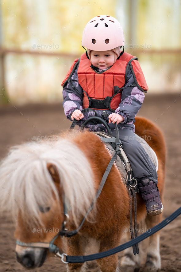 Little Child Riding Lesson. Three-year-old girl rides a pony and does ...