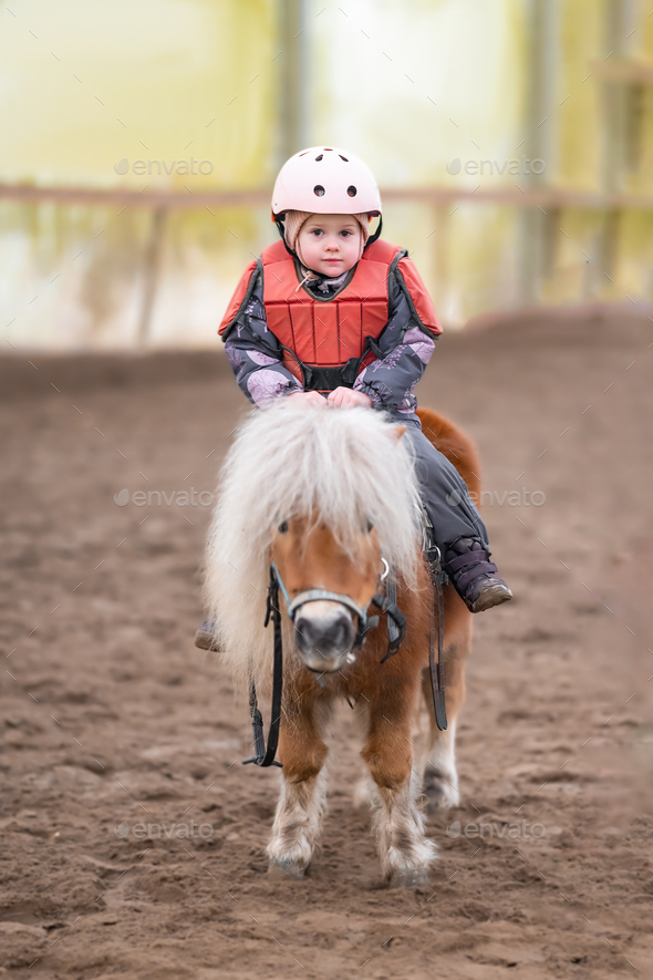 Little Child Riding Lesson. Three-year-old girl rides a pony and does ...