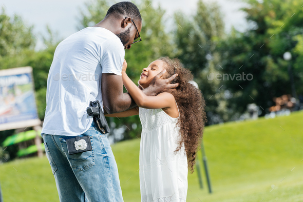 african american police officer and daughter hugging at amusement park ...