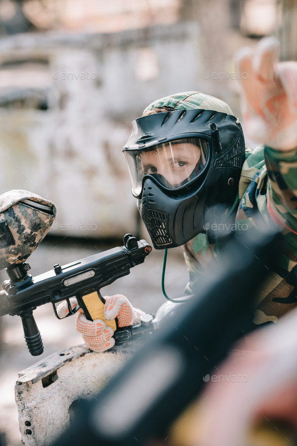 male paintballer in goggle mask and camouflage holding marker gun and ...