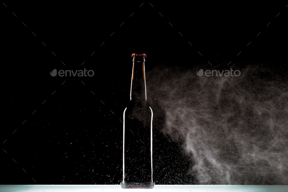 bottle of dark beer with spraying water around at surface on black ...