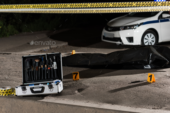 case with investigation tools, car, police line and corpse in body bag ...