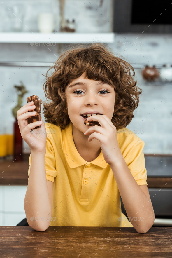 cute happy boy eating delicious chocolate with nuts and smiling at ...