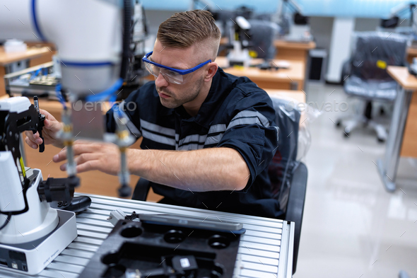 Engineer sitting in robot fabrication room quality checking robot arm ...