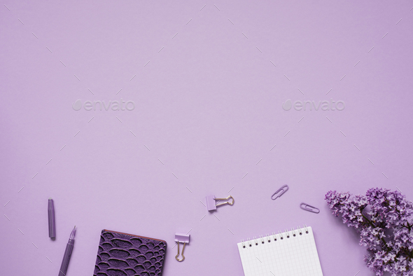 Workplace with notepad, pen, stationery and lilac flowers on a purple ...