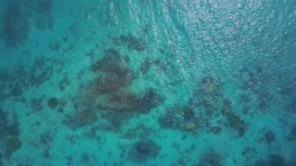 Aerial tracking shot directly down on clear blue waters and coral reefs ...