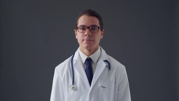 Studio portrait of young professional medical doctor standing over grey ...