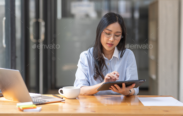 Beautiful young Asian woman working on laptop computer while sitting at ...