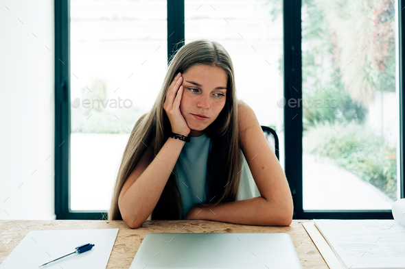 sad and bored female student looking down at the desk with closed ...