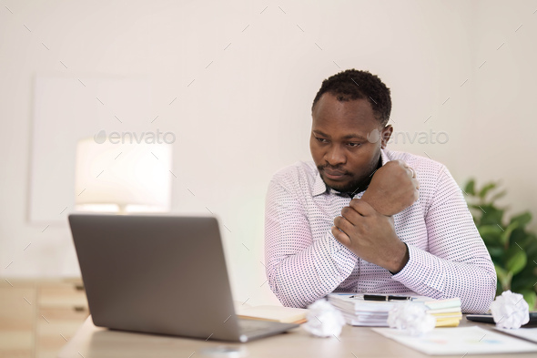 Young african man working at the office using computer laptop suffering ...