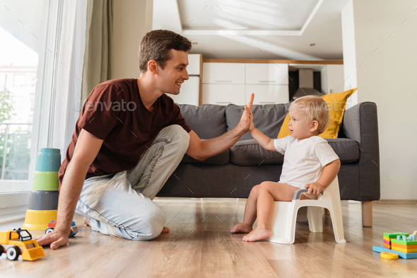 Father assisting his little boy sitting on pot in potty training giving ...